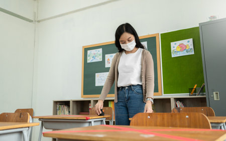 Asian woman Teacher wearing protective face mask using Tape measure on desk in classroom at ...