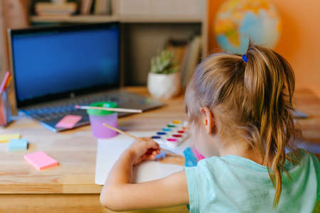 Elementary female student studying online drawing from home using ...