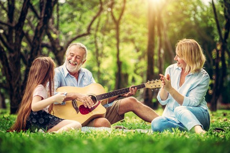 Happy family play guitar and sing together while sitting in the park in ...