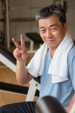 healthy, happy senior man working out in gym, giving no.2 finger ...