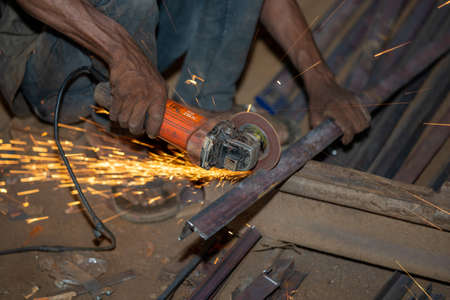 Close-up of busy welder in apron rough grinding metal piece with rotary ...