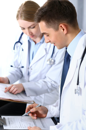 Doctors writing papers using clipboard. Physicians discussing ...