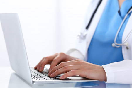 Doctor typing on laptop computer while sitting at the glass desk in ...