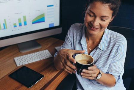 Young businesswoman sitting at her desk and drinking coffee in office ...