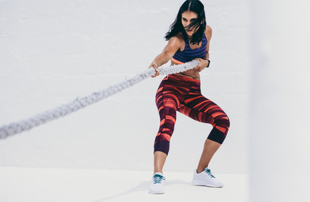 Female athlete pulling a battle rope. Woman in fitness wear doing ...