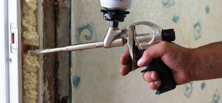 a man's hand with an assembly gun, foaming a gap in a door frame ...