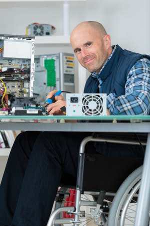 disabled worker in wheelchair fixing a computer - Stock Image - Everypixel