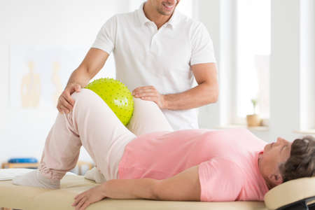 Senior woman holding yellow ball between her knees during physical ...
