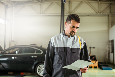 Mechanic looking at service paper in garage. - Stock Image - Everypixel