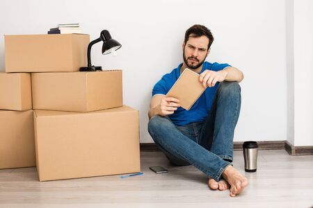 tired young man lying on the floor with packing boxes near and coffee ...