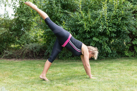 Side view of athletic senior blond woman in forward bend pose with ...