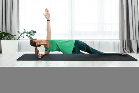 Calm young woman standing in plank position on fitness mat, spending ...