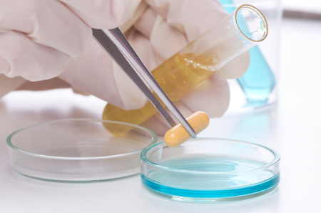 Close up of scientist's hands holding capsule with tweezers and test ...