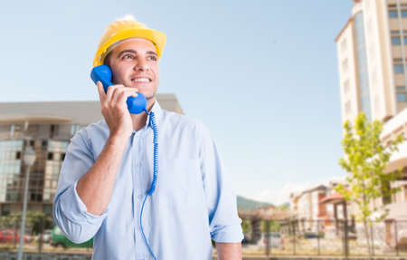 Smiling engineer with protection helmet talking outside on telephone ...