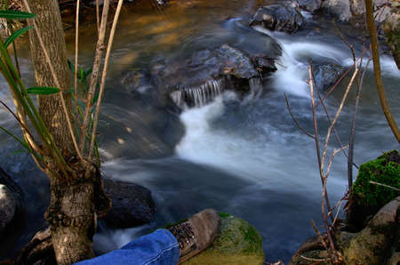 A mountain river flowing through stones and a boot of a hiking Water is ...