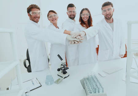 successful team of young scientists with hands clasped together ...