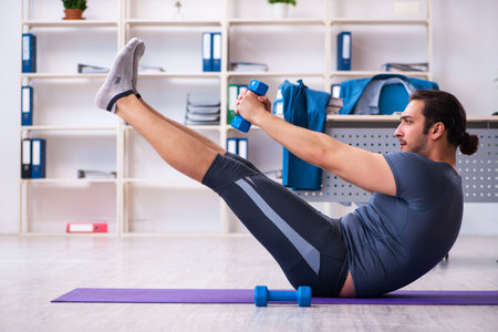Young handsome employee doing sport exercises in the office - Stock ...