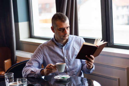 Elegant man reading a book and drinking coffee on the table in a ...