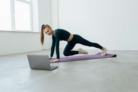 Fit woman doing yoga exercise while watching tutorial on laptop at home ...