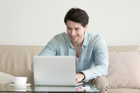Young handsome man smiling looking at screen of laptop computer ...