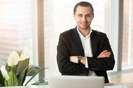 Portrait of young smiling guy in formal wear sitting at work desk in ...