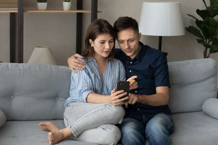 Happy bonding loving young Caucasian couple using smartphone at home ...