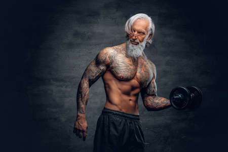 Bearded old man bodybuilder with tattoos holding dumbbell - Stock Image ...