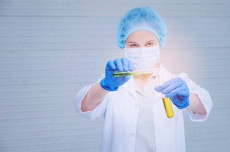 young female scientist in protective mask and gloves dropping yellow ...