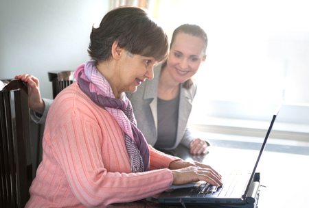 Younger woman helping an elderly person using laptop computer for ...