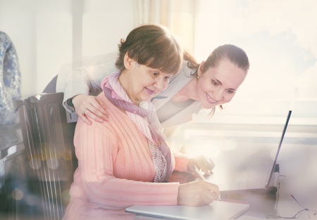 Younger woman helping an elderly person using laptop computer for ...