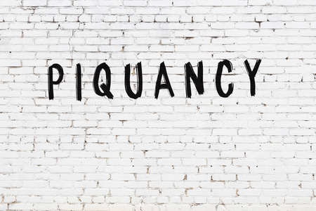 White brick wall with inscription piquancy handwritten with black paint ...