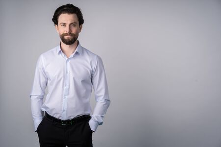 A grown man with a beard in a white shirt, his two hands in his pockets ...