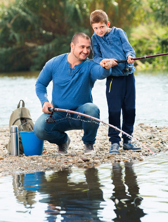 Portrait of glad smiling father and cute son fishing with rods in ...