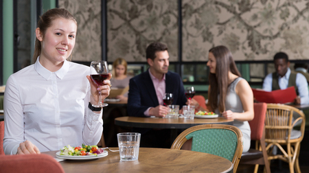 Attractive young woman enjoying diner with glass of red wine alone in ...