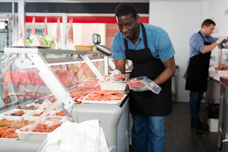 Successful owner of butcher store with his worker preparing fresh meat ...