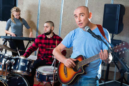 Rehearsal of music group. Smiling band leader playing guitar and ...