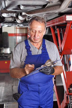 Confident male car mechanic at the workshop writing job sheet for ...