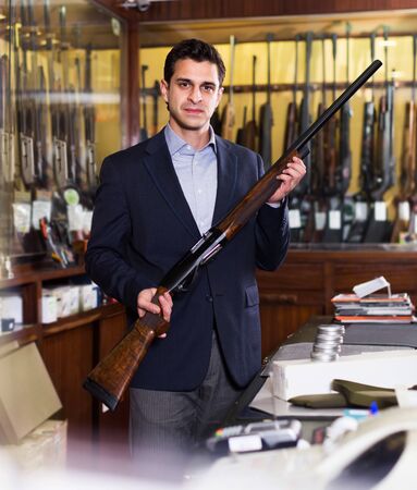 Portrait of positive salesman in gun shop holding shotgun - Stock Image ...
