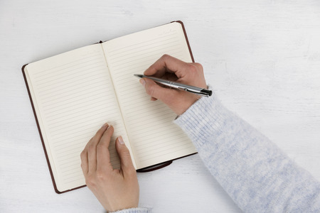 Woman writing in a blank open diary, notebook or journal with a ...