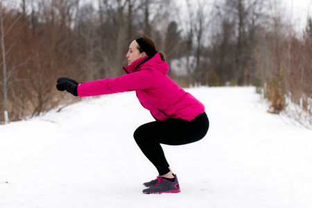 Fit woman doing squats exercises on outdoor winter nature trail ...