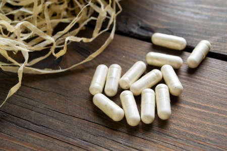 ON a wooden background capsules with herbs, and next to dry grass. Dry ...