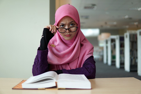 A beautiful Muslimah student sitting in the library with book open on ...