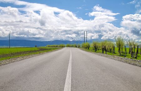 Asphalt road in spring against the background of mountains and sky ...