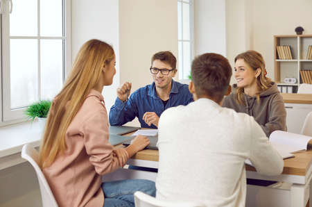 Group of happy smart college or university students sitting around desk ...