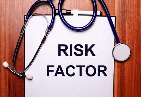 The word RISK FACTOR is written on white paper on a wooden background ...