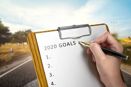 Human hand writes a list for 2020 goals in the paper on clipboard ...