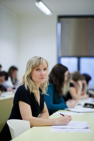 young pretty female college student sitting in a classroom full of ...