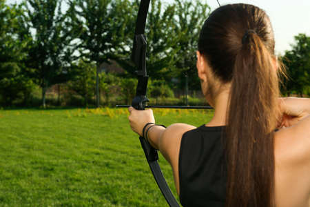 Woman with bow and arrow practicing archery in park, back view - Stock ...