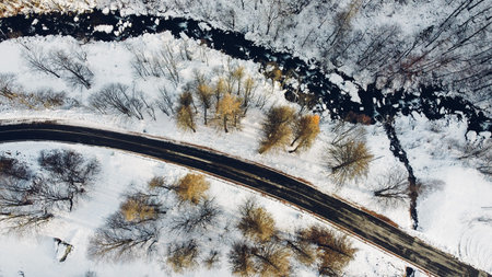 Aerial high angle view of mountain road, trees and river under the snow ...