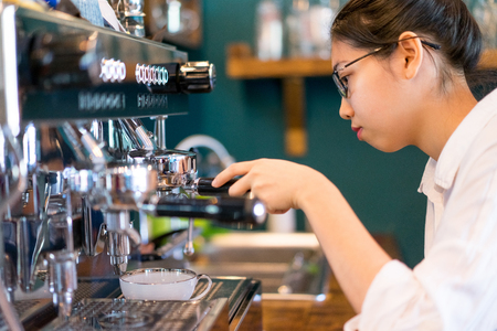 Concentrated Asian female barista making coffee using espresso machine ...